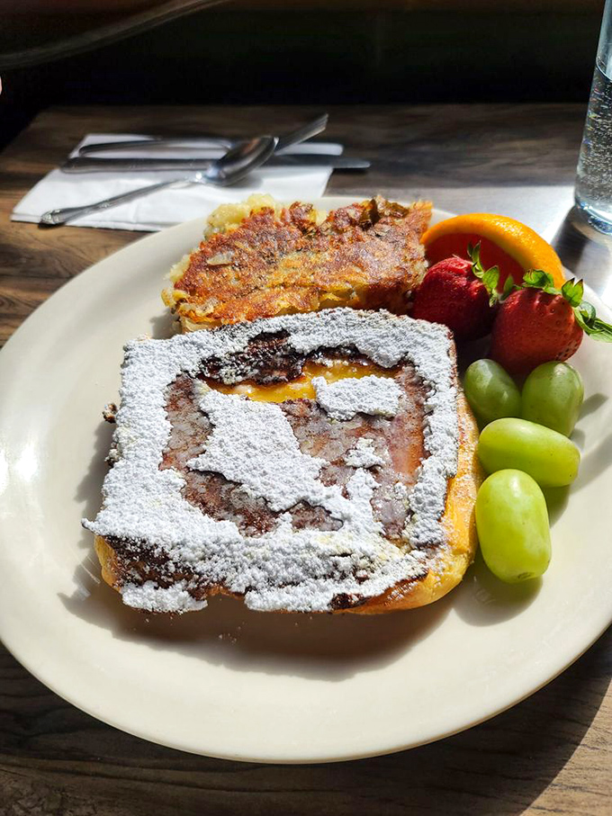 Behold the star attraction: French toast dusted with powdered sugar like fresh snow, surrounded by a colorful fruit entourage that makes mornings worth waking up for.
