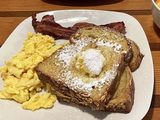 French toast dusted with powdered sugar, a pat of butter melting into golden perfection, alongside eggs scrambled just right and bacon that means business.