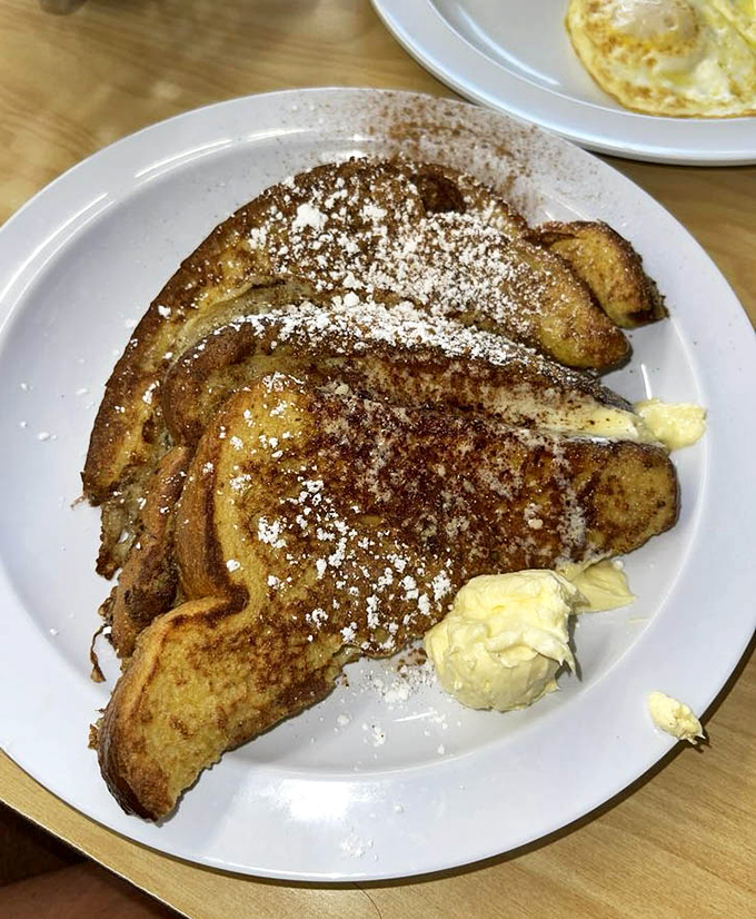 Golden French toast arrives dusted with powdered sugar, looking like breakfast royalty ready for its close-up.