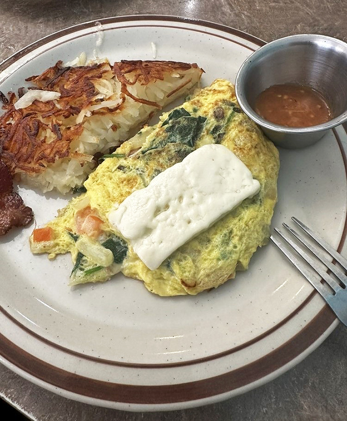 The legendary Greek omelet arrives like a yellow pillow of possibility, stuffed with veggies and topped with feta that means business.