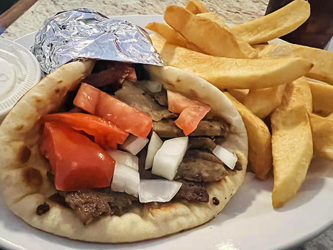Behold the gyro in its natural habitat – perfectly seasoned meat, fresh veggies, and a pita that somehow manages to be both sturdy and tender. The French fries are just showing off.