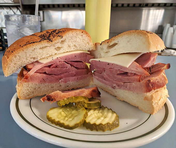 Behold the masterpiece: paper-thin slices of pink perfection stacked generously between fresh bread with pickle coins standing guard. This is sandwich minimalism at its finest.