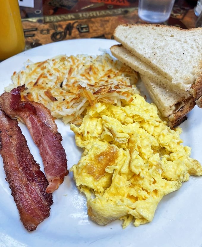 Breakfast perfection on a plate: golden scrambled eggs, crispy hash browns, and bacon cooked just right&mdash;the holy trinity of morning satisfaction.