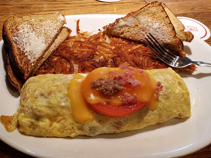 This omelet doesn't just sit on the plate—it commands attention. Golden perfection wrapped around melty cheese with hash browns that achieved the crispy-fluffy paradox.