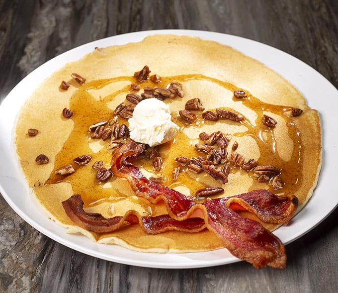 Pancake perfection: a golden disc the size of a hubcap, topped with butter, pecans, syrup, and bacon. Breakfast architecture at its finest.