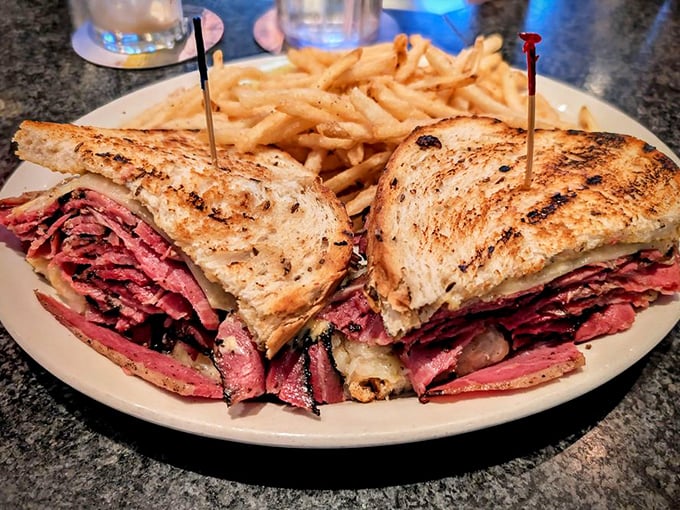 The Reuben in its natural habitat &ndash; gloriously stacked, perfectly toasted, and flanked by golden fries. This isn't a sandwich; it's an architectural masterpiece.