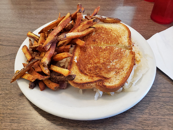The Reuben arrives like a golden-brown promise of satisfaction, with crispy fries standing guard beside the sandwich's melty, savory perfection.