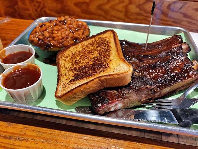 Ribs that surrender from the bone with dignified restraint, served with Texas toast and beans that clearly attended finishing school.