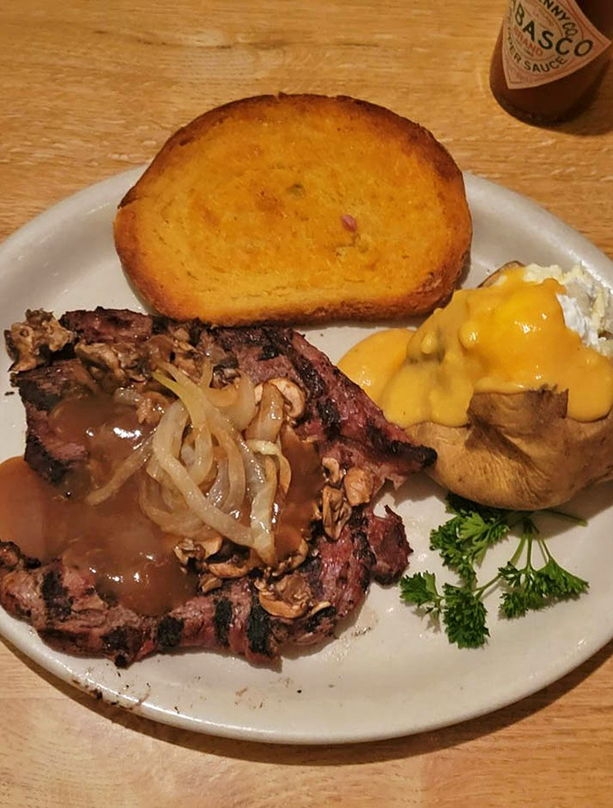 Behold the star of the show: a perfectly charred ribeye with saut&eacute;ed onions, alongside a cheese-smothered baked potato and golden garlic toast.