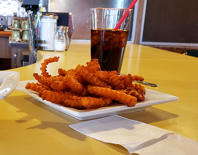 Sweet potato fries that crunch like autumn leaves, served alongside a frosty cola in a classic diner setting that screams "American comfort." 