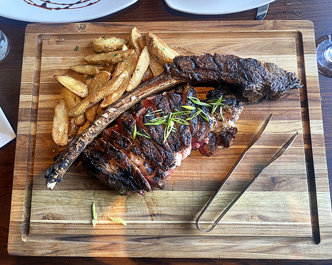 The Tomahawk steak arrives like a prehistoric indulgence on a wooden battlefield, flanked by golden fries and ready for conquest.