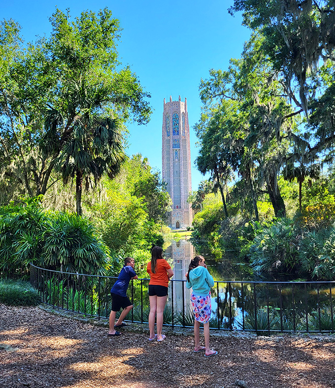 Three young visitors discover the perfect reflection spot, where tower meets water in a mirror image that doubles the wonder.