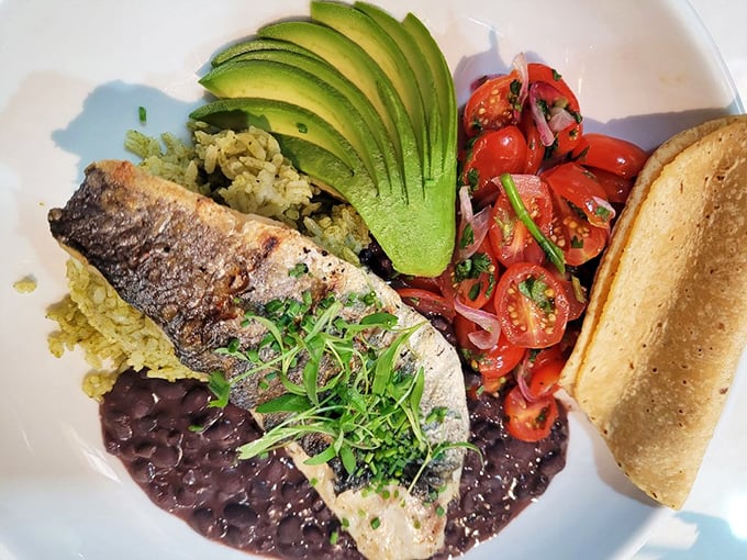 A perfectly grilled fish rests on a bed of cilantro rice and black beans, with sliced avocado and pico de gallo standing by like loyal companions.