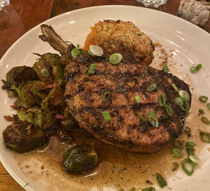 The star of the show: a perfectly seared pork chop nestled alongside Brussels sprouts, with scallions adding a fresh finish to this masterpiece.