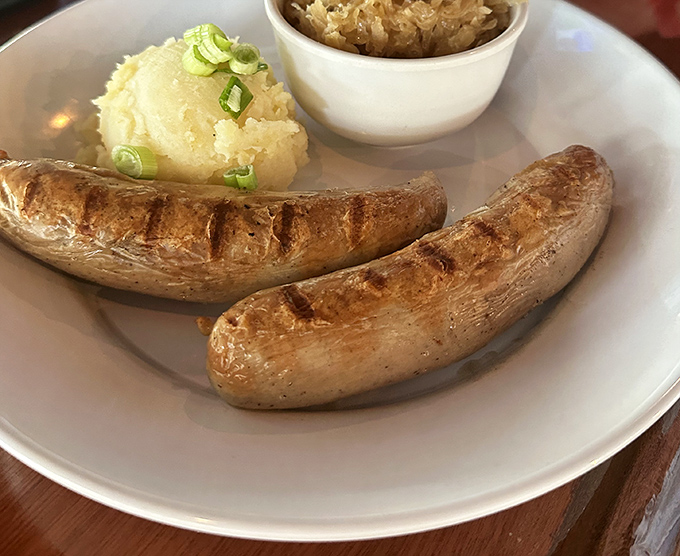 Two perfectly grilled bratwursts nestled beside creamy mashed potatoes and sauerkraut&mdash;comfort food that speaks a universal language of deliciousness.