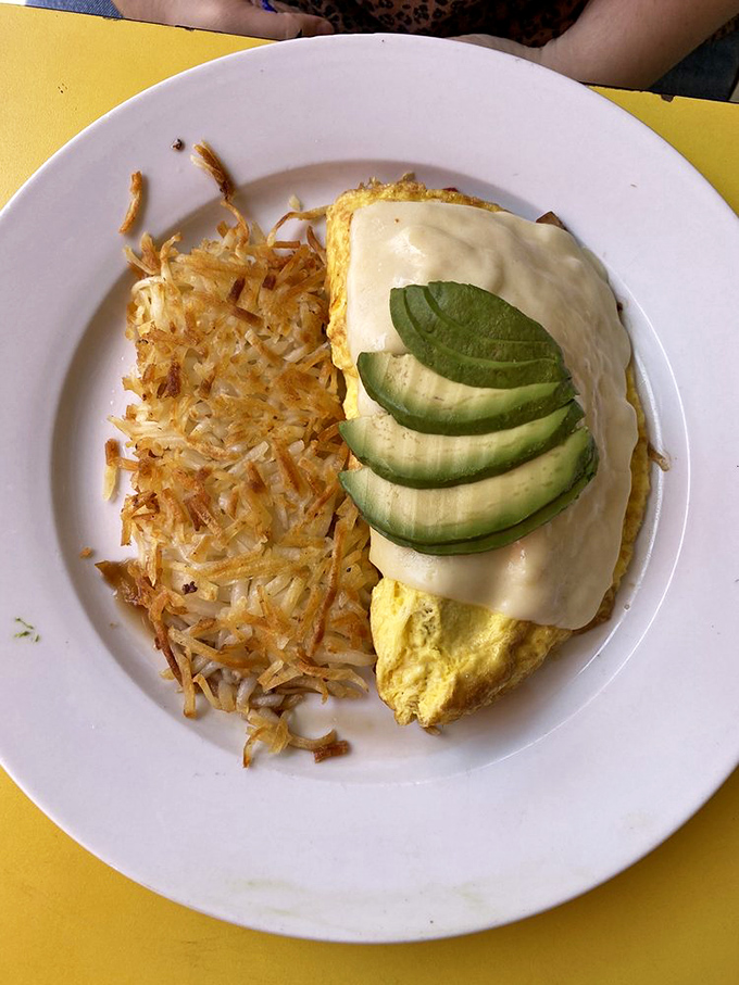 This omelet doesn't just come with avocado—it's adorned with it, like a crown jewel atop a golden pillow of perfectly cooked eggs.