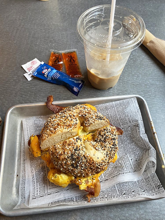 That everything bagel sandwich is wearing more seeds than a bird feeder convention, and the iced coffee looks like it could jumpstart a Monday.