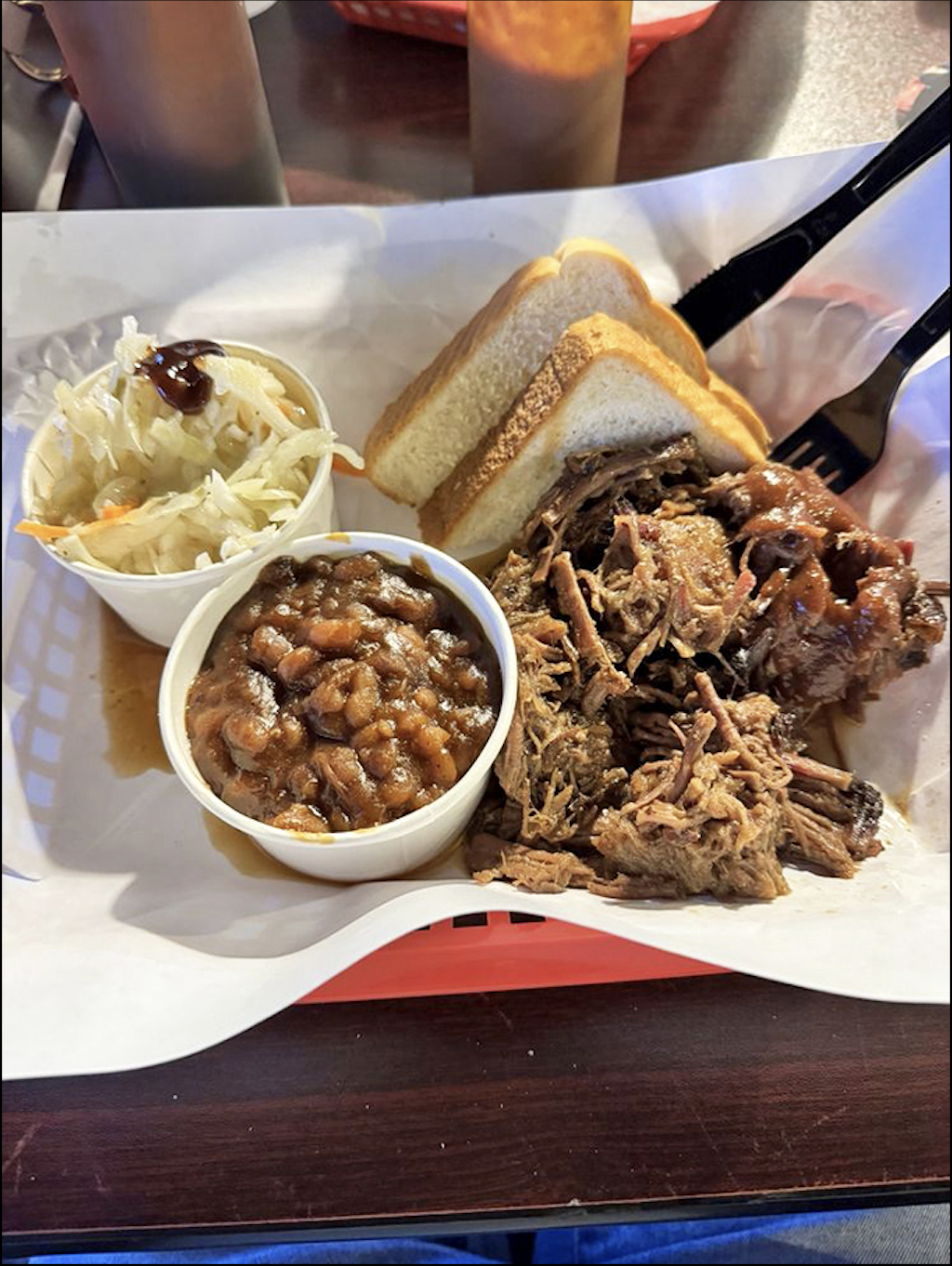 Behold the holy trinity of BBQ perfection: pulled pork sandwich flanked by creamy coleslaw and beans. The bread's just there to keep your fingers clean.