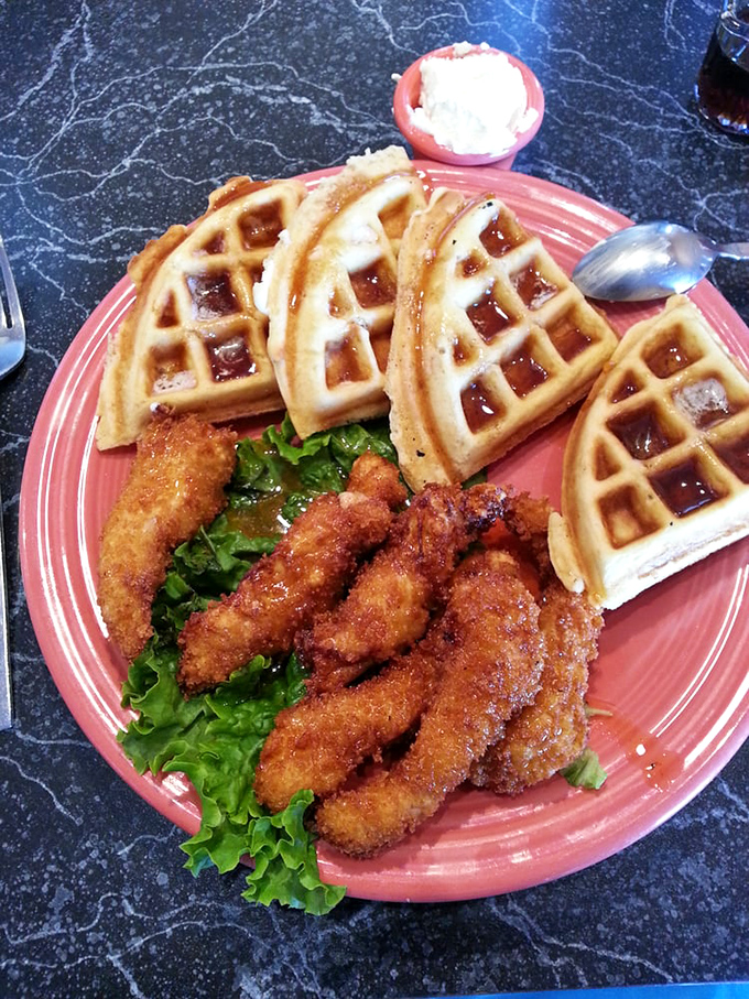 Golden waffles cradle perfectly crispy chicken strips on a coral plate&mdash;a sweet and savory duet that makes breakfast feel like the main event.