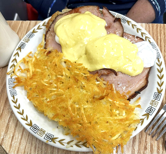 Behold the star attraction! Golden hollandaise cascades over perfectly poached eggs and Canadian bacon, with crispy hash browns standing guard.