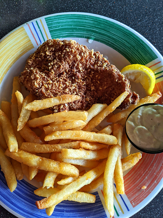 Golden-battered fish perched atop a mountain of crispy fries &ndash; this isn't just fish and chips, it's edible sunshine on a colorful plate. 