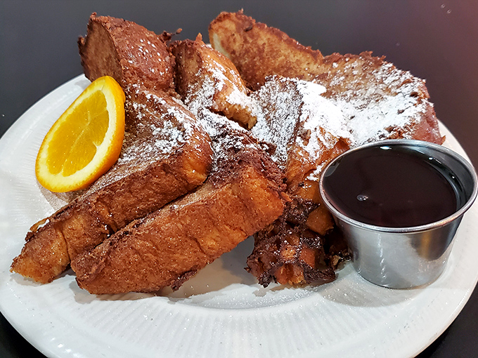French toast nirvana achieved! Golden-brown perfection with a dusting of powdered sugar that melts into each crevice. The orange slice isn't just garnish—it's an invitation.
