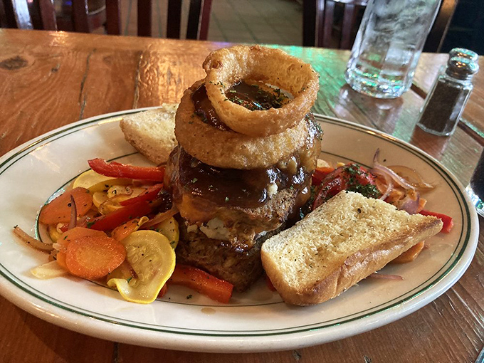 Not just meatloaf—a towering monument to comfort food architecture, complete with a crispy onion ring crown and vegetable subjects paying tribute.