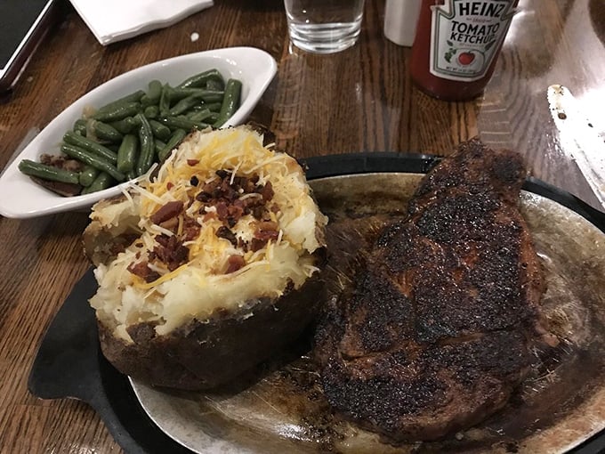 Behold the star of the show – a perfectly crusted ribeye alongside a loaded twice-baked potato and green beans. Meat poetry on a sizzling plate.