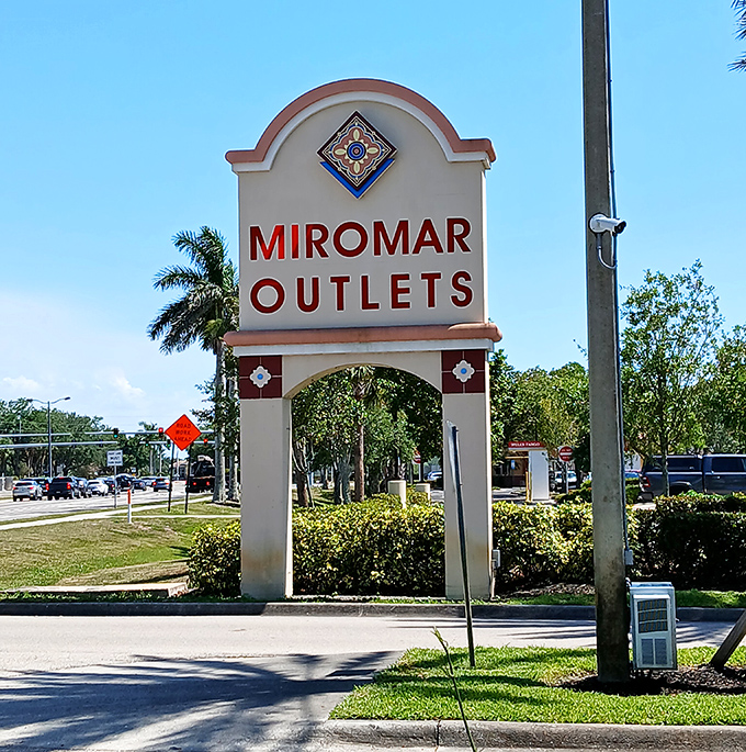 Miromar's entrance sign stands tall against the blue sky, like a retail lighthouse guiding bargain hunters to discount shores.