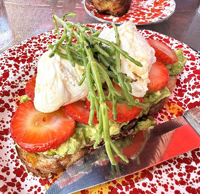 Avocado toast gets the royal treatment with poached eggs, strawberries, and sea beans creating a breakfast masterpiece on a speckled plate.