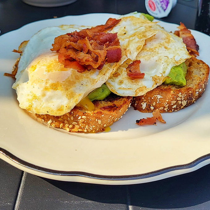 Breakfast perfection on a plate: eggs, avocado, and bacon on seeded toast. Morning fuel that would make even non-morning people set their alarms earlier.