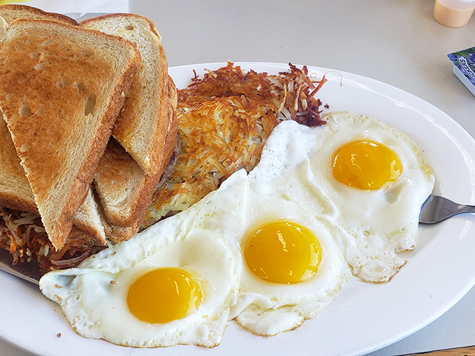 Three sunny-side-up eggs stand at attention next to golden hash browns and toast&mdash;breakfast doesn't get more honest than this.