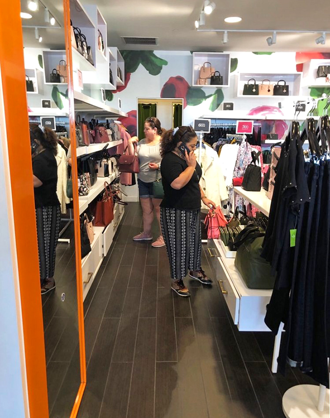 Shoppers navigate a Kate Spade boutique with the focused determination of treasure hunters, each handbag a potential trophy to bring home.