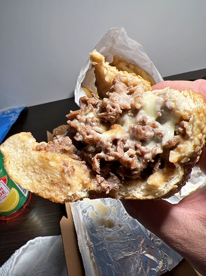 The cheesesteak in mid-bite reveals its true character: perfectly chopped meat embraced by melted cheese in a passionate sandwich romance.