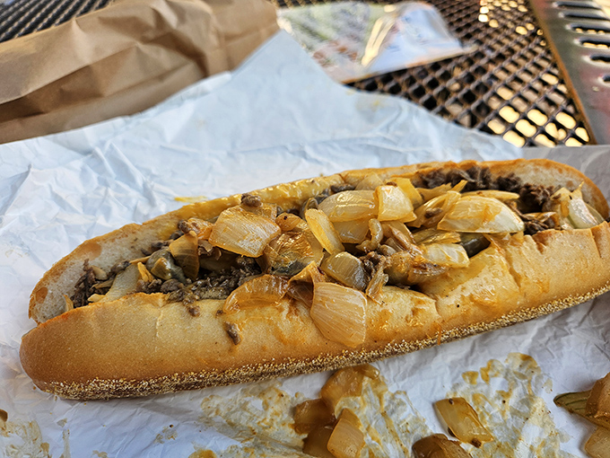 The cheesesteak in its natural habitat: wrapped in paper, oozing with caramelized onions, ready to change your definition of sandwich perfection.