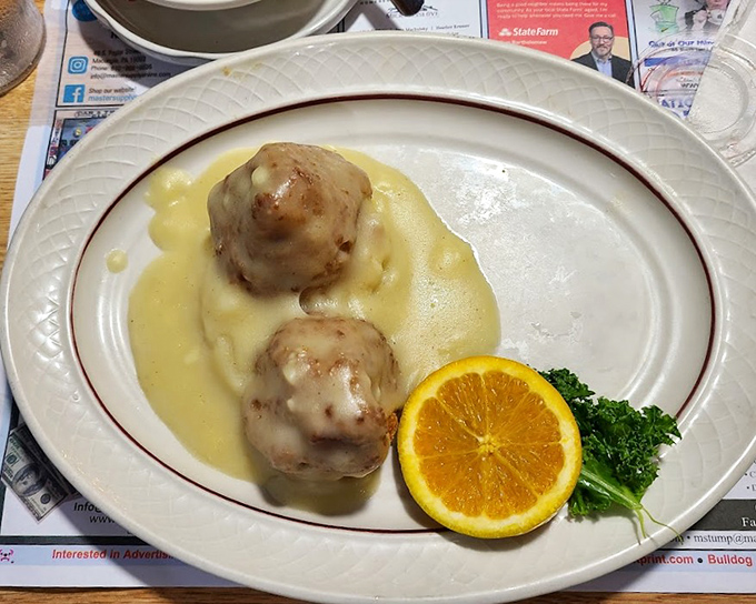 Chicken croquettes lounging in creamy sauce like they're at a spa retreat. The orange slice isn't just garnish—it's a pop of color saying "this isn't your average comfort food."