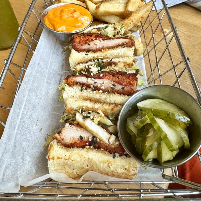 The chicken katsu sandwich arrives like a crispy ambassador of joy, flanked by its loyal sidekicks: pickles and dipping sauce.