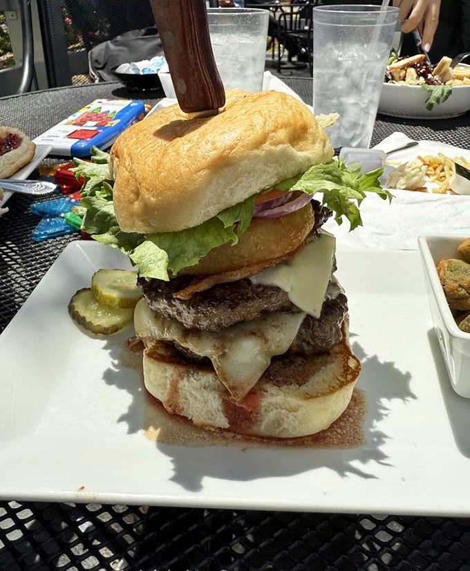 This towering burger achievement should come with its own building permit &ndash; layers of beef, cheese, and veggies that defy both gravity and restraint.