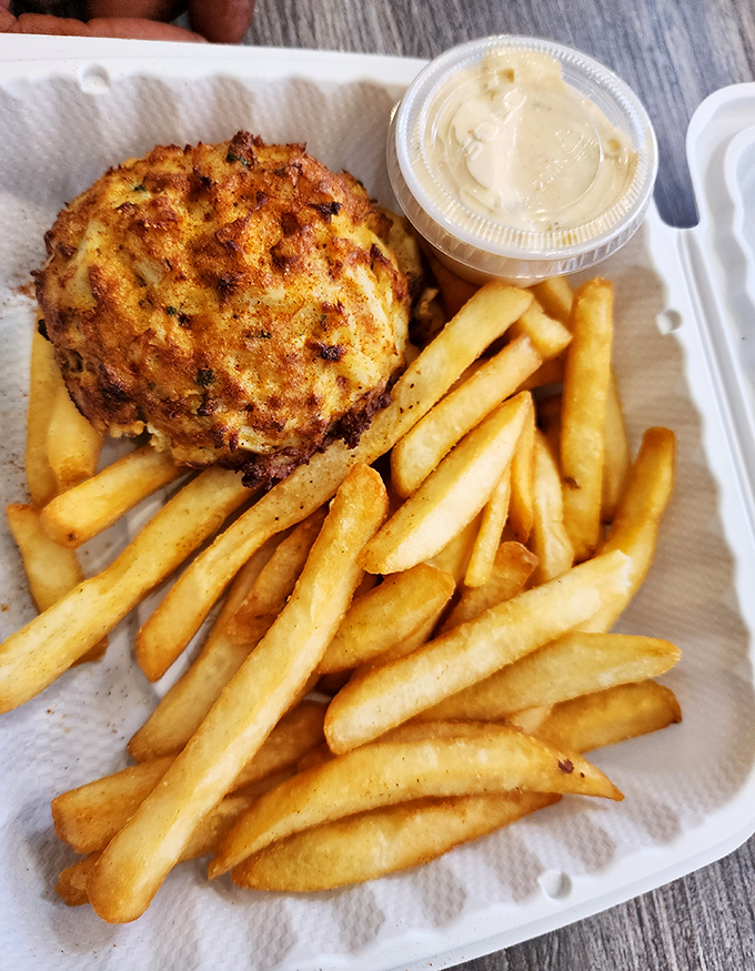 This golden crab cake sits like edible treasure next to crispy fries and creamy sauce perfection.