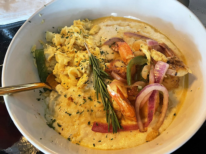 Grits and shrimp having their best day ever, with a sprig of rosemary standing guard like it knows something special is happening.