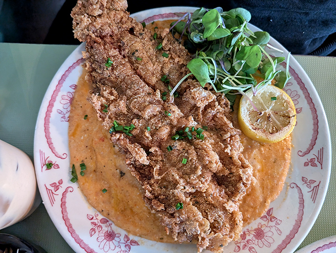 The Fish N Grits arrives like edible artwork &ndash; crispy catfish perched atop creamy grits, with that roasted pepper sauce creating a pool of pure flavor bliss.