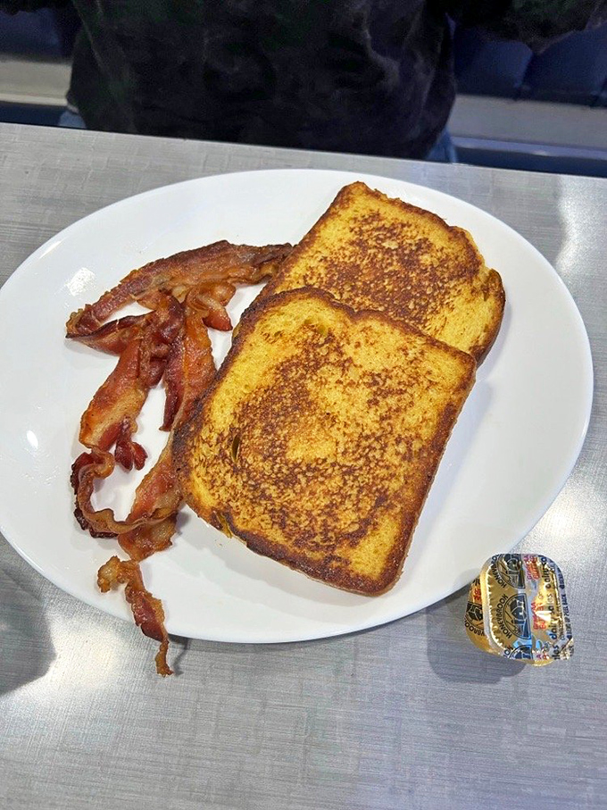 Golden-brown French toast with a side of perfectly crispy bacon &ndash; breakfast's greatest hits album on a single white plate.