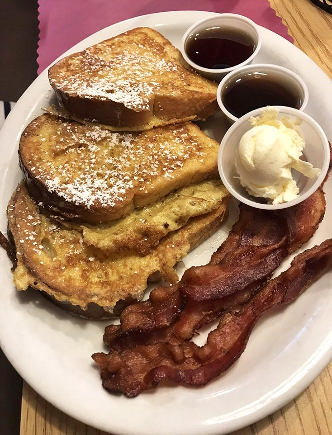 French toast that's dressed for success with powdered sugar, whipped cream, and bacon that's clearly living its best life.