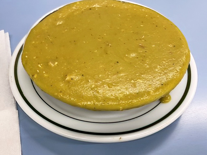 The split pea soup glows with an amber warmth that promises comfort. Each spoonful delivers tiny ham treasures hiding among the peas.