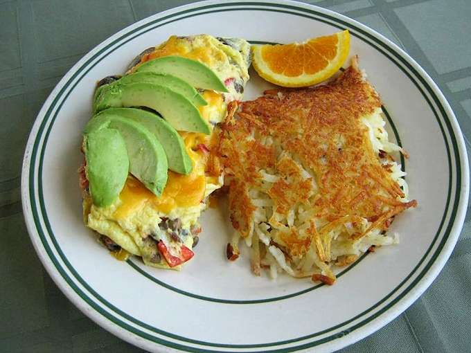 Breakfast alchemy at its finest—an omelet that cradles avocado slices like precious gems, with hash browns crisped to golden perfection.