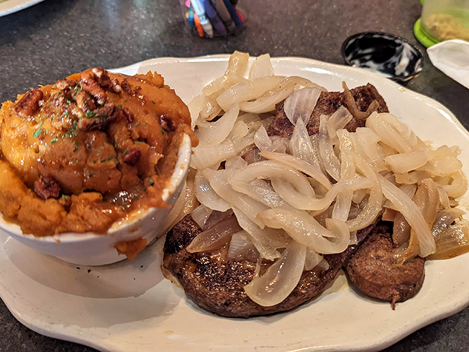 A perfectly seared steak smothered in caramelized onions, paired with what appears to be a side that would make any comfort food enthusiast weak at the knees.