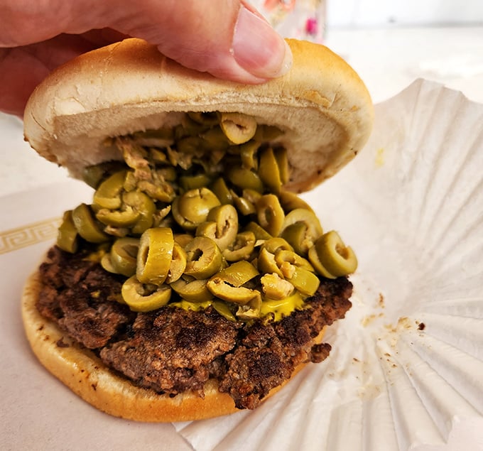 An olive lover's dream come true! Those perfectly sliced green gems cascade over the patty like a savory waterfall of Mediterranean goodness.