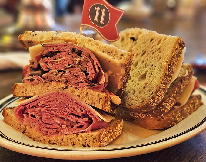 The pastrami sandwich stands tall like a meaty skyscraper between rye bread foundations. That little flag isn't decoration &ndash; it's claiming territory in your heart.