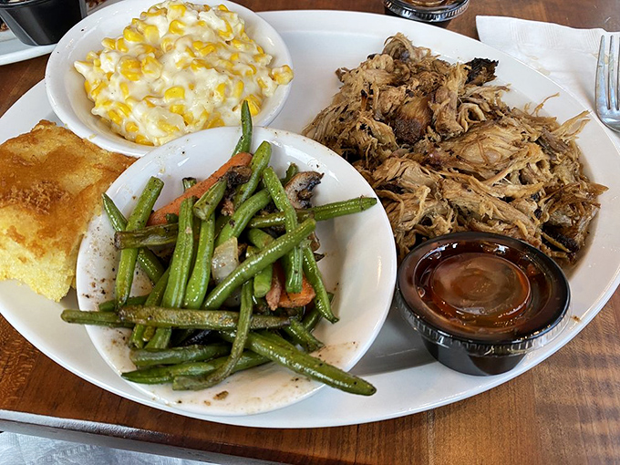 A BBQ trinity: tender pulled pork, garden-fresh green beans, and creamy mac and cheese with cornbread on the side. The holy grail of comfort on a plate.