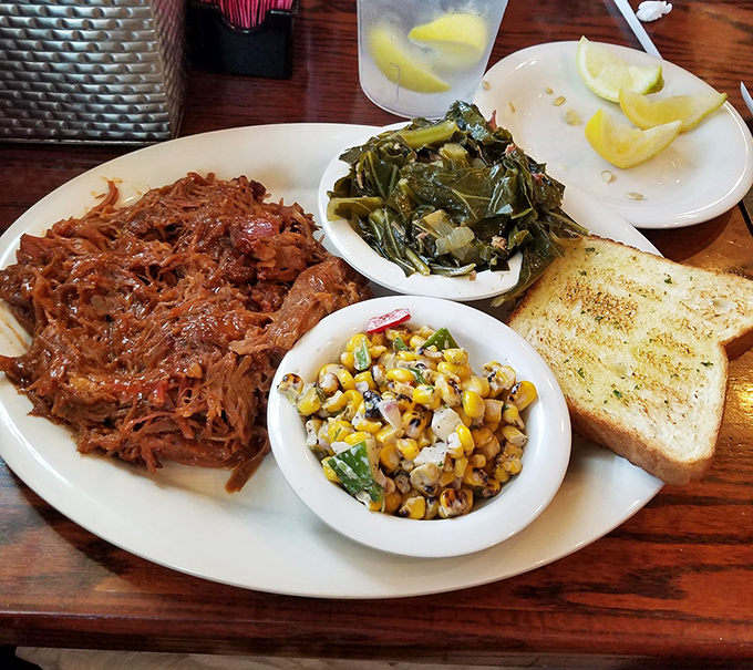 Pulled pork that surrenders at the sight of a fork, paired with collard greens and roasted corn salad – the holy trinity of Southern comfort.